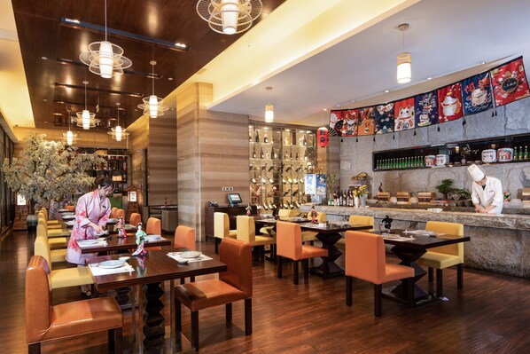 Restaurante com piso de madeira, várias mesas e cadeiras, área de bar e parede decorativa com faixas.