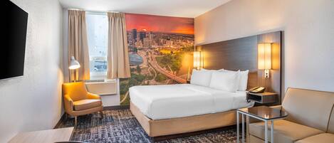 Quarto de hotel com cama, sofá, escrivaninha, cadeira, luminária, mesa de cabeceira e um mural com vista para a cidade na parede.