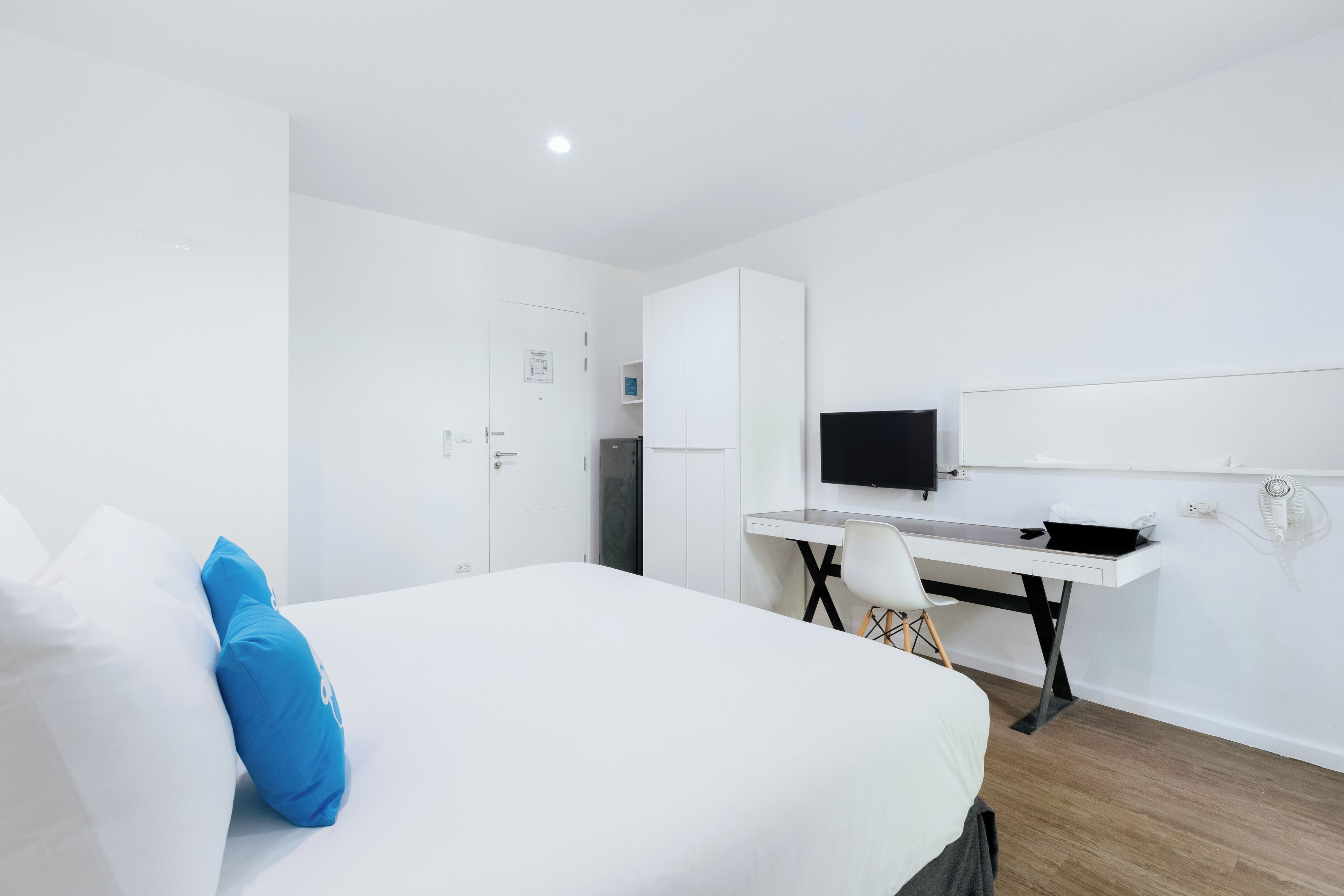 Quarto de hotel com cama, escrivaninha, cadeira e televisão.