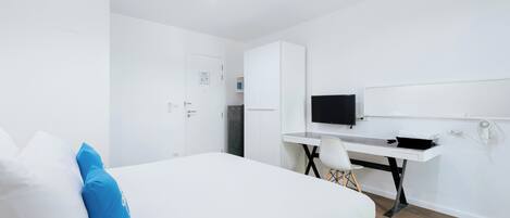 Quarto de hotel com cama, escrivaninha, cadeira e televisão.