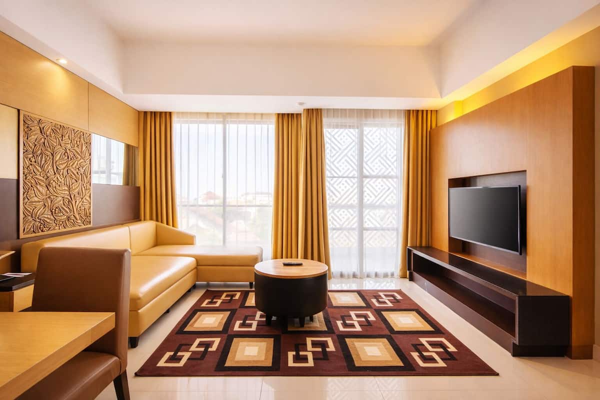 Quarto de hotel moderno com sofá, mesa de centro, televisão e tapete estampado.