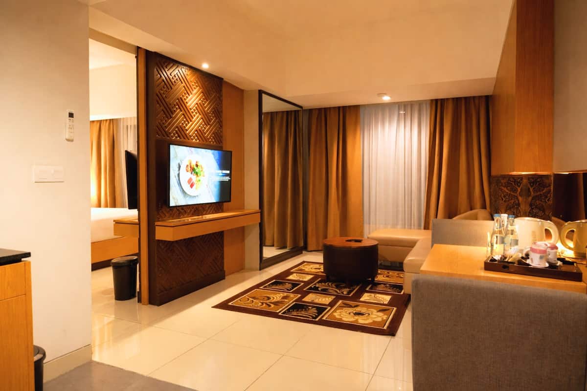 Quarto de hotel com televisão, sofá, mesa de centro e tapete decorativo.
