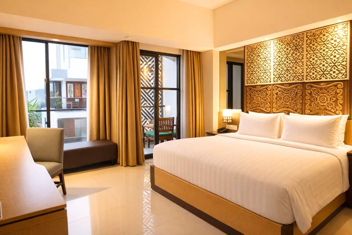 Quarto de hotel com uma cama grande, uma escrivaninha, uma cadeira, varanda com vista e cabeceira decorativa.