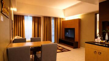 Quarto de hotel com área de refeições, televisão, armário de madeira e janela com cortinas.