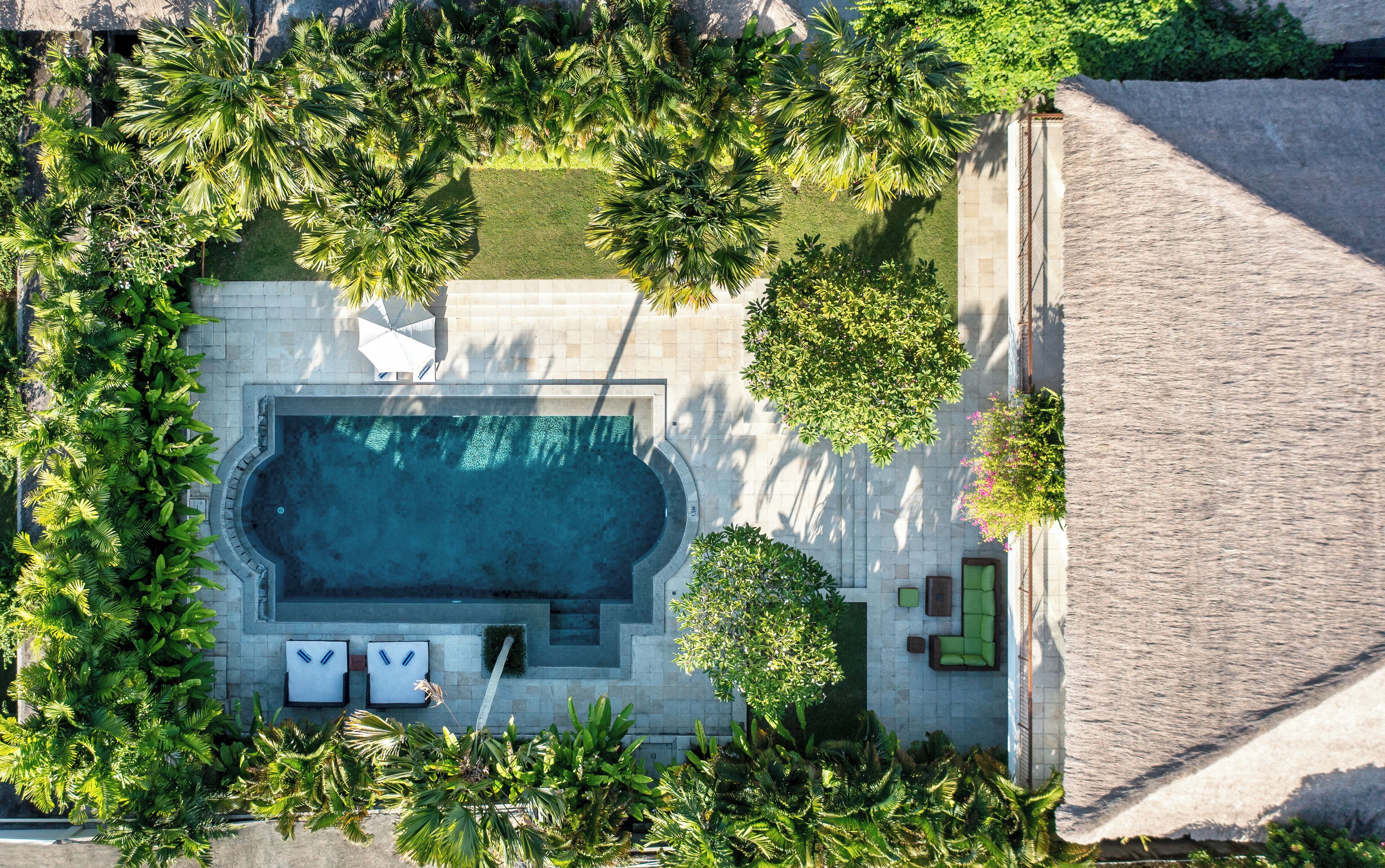 Vista aérea de uma piscina cercada por vegetação exuberante, com uma estrutura de telhado de palha à direita.