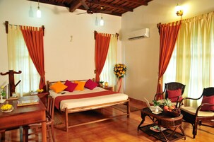 Quarto bem mobiliado com cama, escrivaninha, cadeiras e uma pequena mesa com frutas e um laptop.