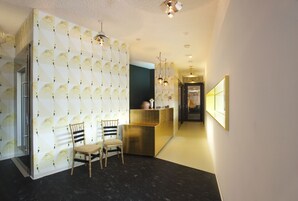 Uma área de recepção com balcão, duas cadeiras, papel de parede estampado e iluminação pendente.