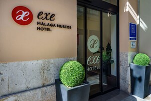 Exterior do Hotel Exe Málaga Museos com design moderno, incluindo logotipo, nome e entrada de vidro.