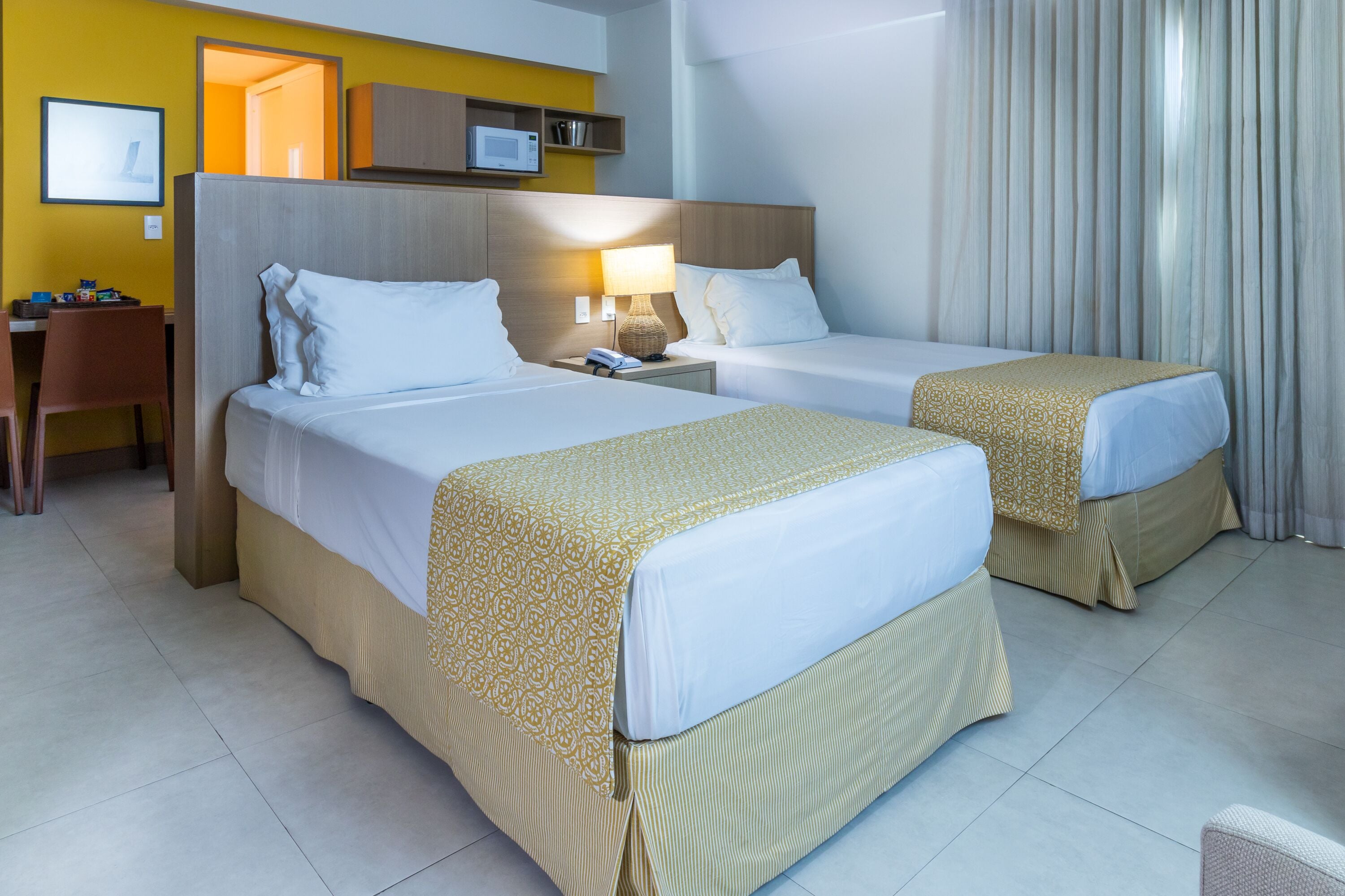 Quarto de hotel com duas camas, uma escrivaninha e televisão na parede.