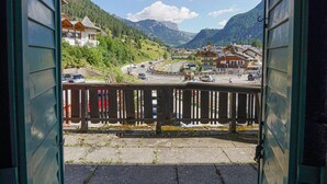 A porta aberta dá para uma varanda com vista para uma paisagem montanhosa, com edifícios e uma estrada.