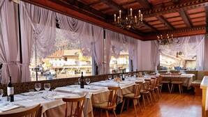 Restaurante com mesas preparadas para refeições, cadeiras de madeira e vista para um edifício através de grandes janelas.