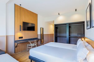 Quarto de hotel moderno com uma cama grande, uma escrivaninha com televisão de tela plana, um espelho e um guarda-roupa com aquecedor embutido.