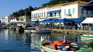Um porto com barcos atracados, um café à beira-mar e edifícios com toldos azuis.