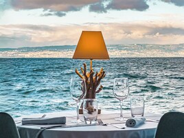 Mesa posta para refeição, com vista para o mar e paisagem urbana ao fundo.