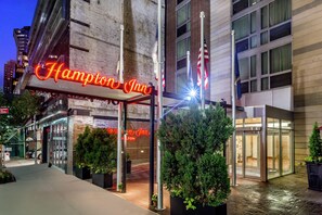 Entrada de hotel com letreiro de neon, bandeiras americanas e fachada de tijolos.