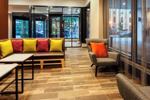 Um hall moderno com piso de madeira, um sofá com almofadas coloridas, uma poltrona e uma porta de vidro que dá para o exterior.
