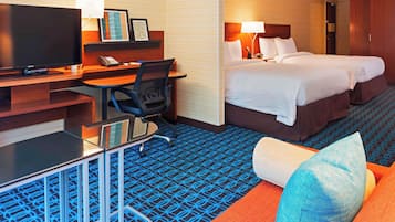 Quarto de hotel com cama, escrivaninha com televisão, cadeira e sofá.