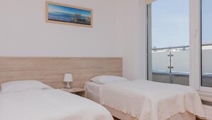 Quarto de hotel com duas camas, cabeceira de madeira, mesa de cabeceira com abajur e uma grande janela com vista para o mar.