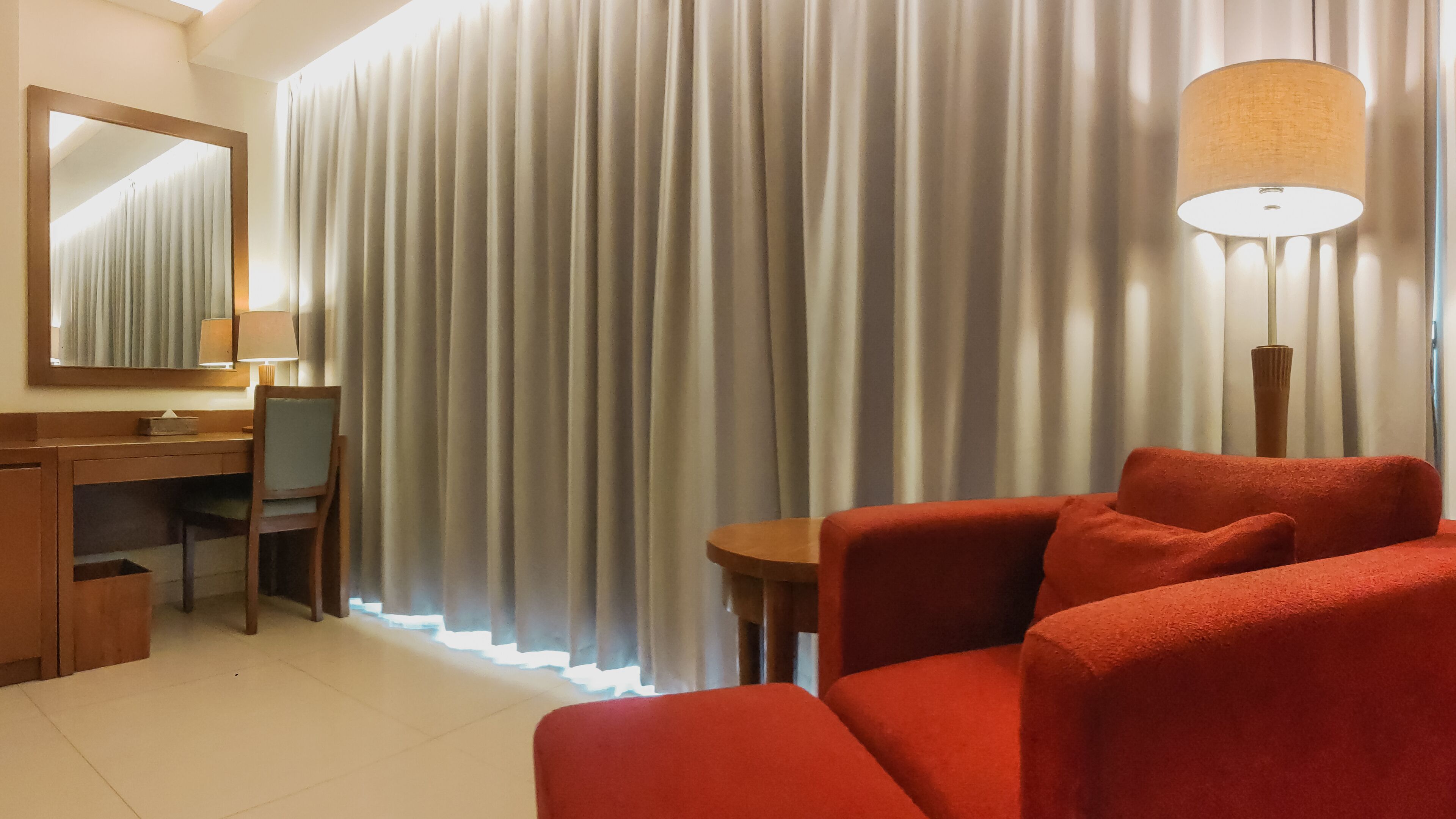 Quarto de hotel com escrivaninha, cadeira e sofá vermelho.