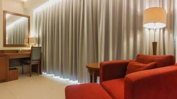 Quarto de hotel com escrivaninha, cadeira e sofá vermelho.