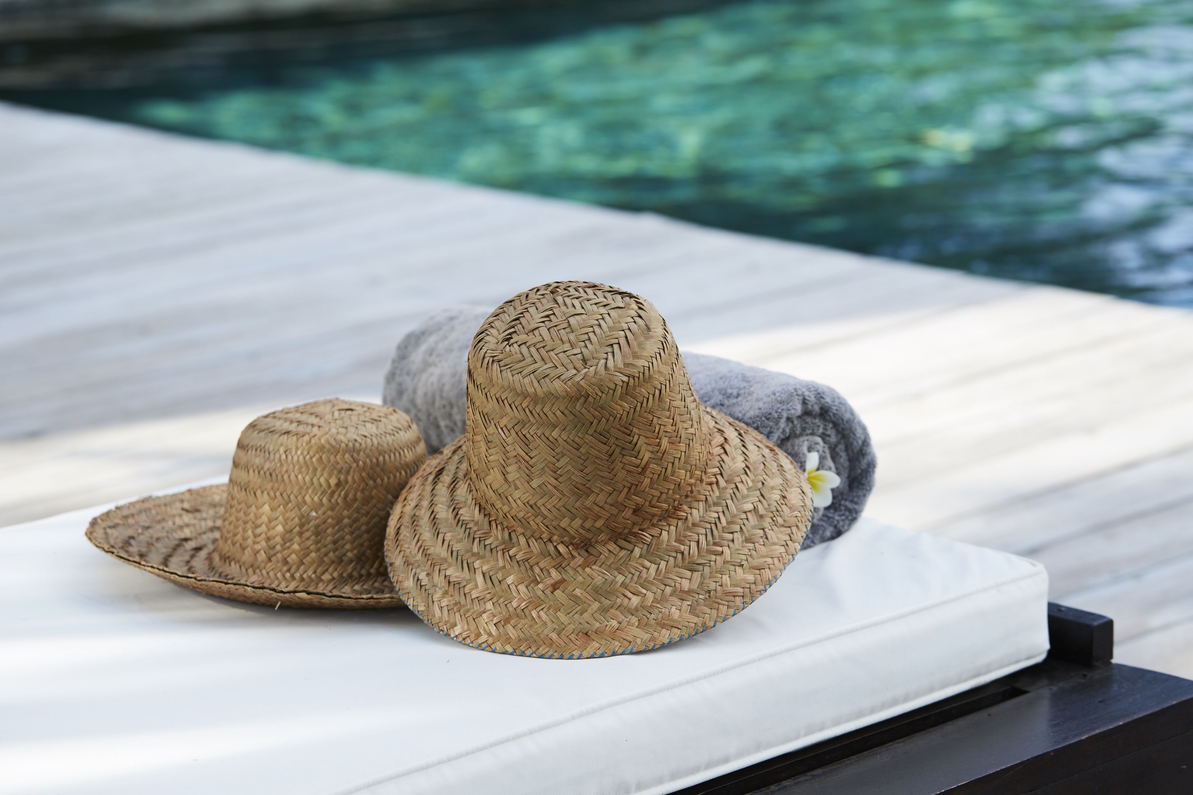 Dois chapéus de palha sobre uma superfície branca perto de uma piscina.