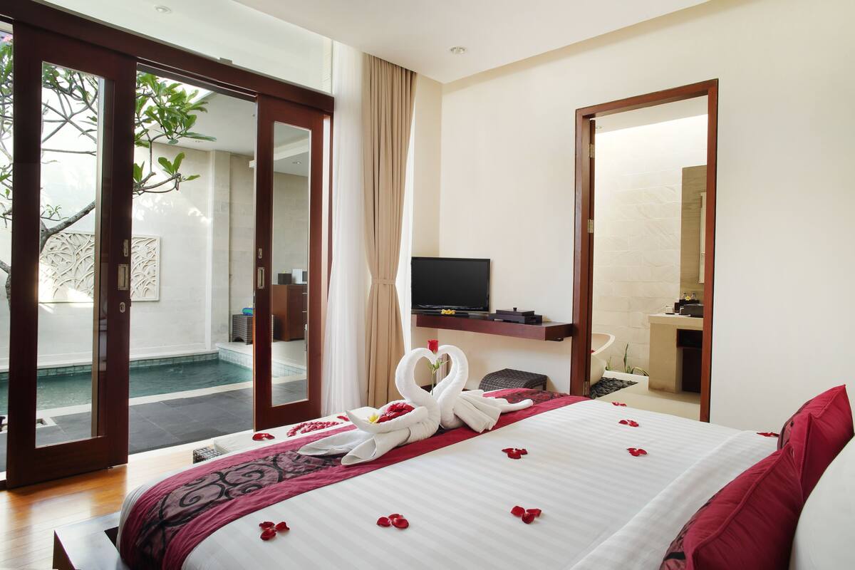 Quarto de hotel com cama, televisão, banheiro e área de piscina.