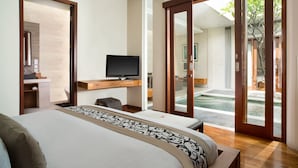 Quarto de hotel moderno com uma cama grande, televisão, secretária de madeira e porta de vidro deslizante para uma área de piscina.