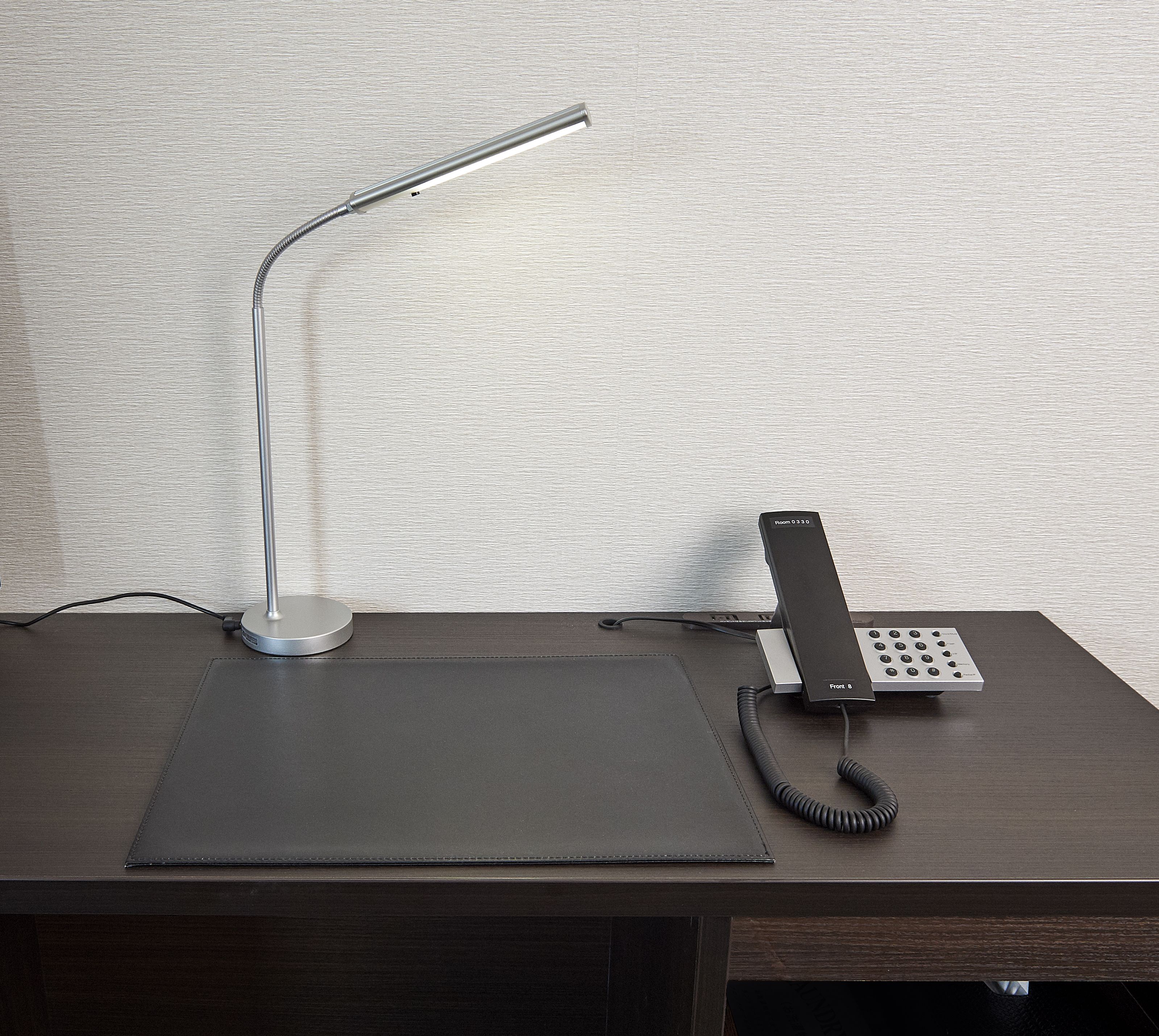 Uma mesa com luminária, telefone e régua de tomadas.