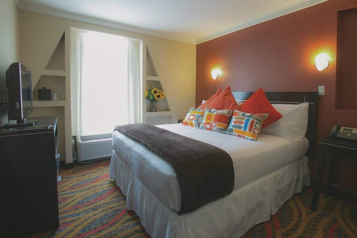 Quarto de hotel com cama, escrivaninha, cadeira, televisão e janela com vista.