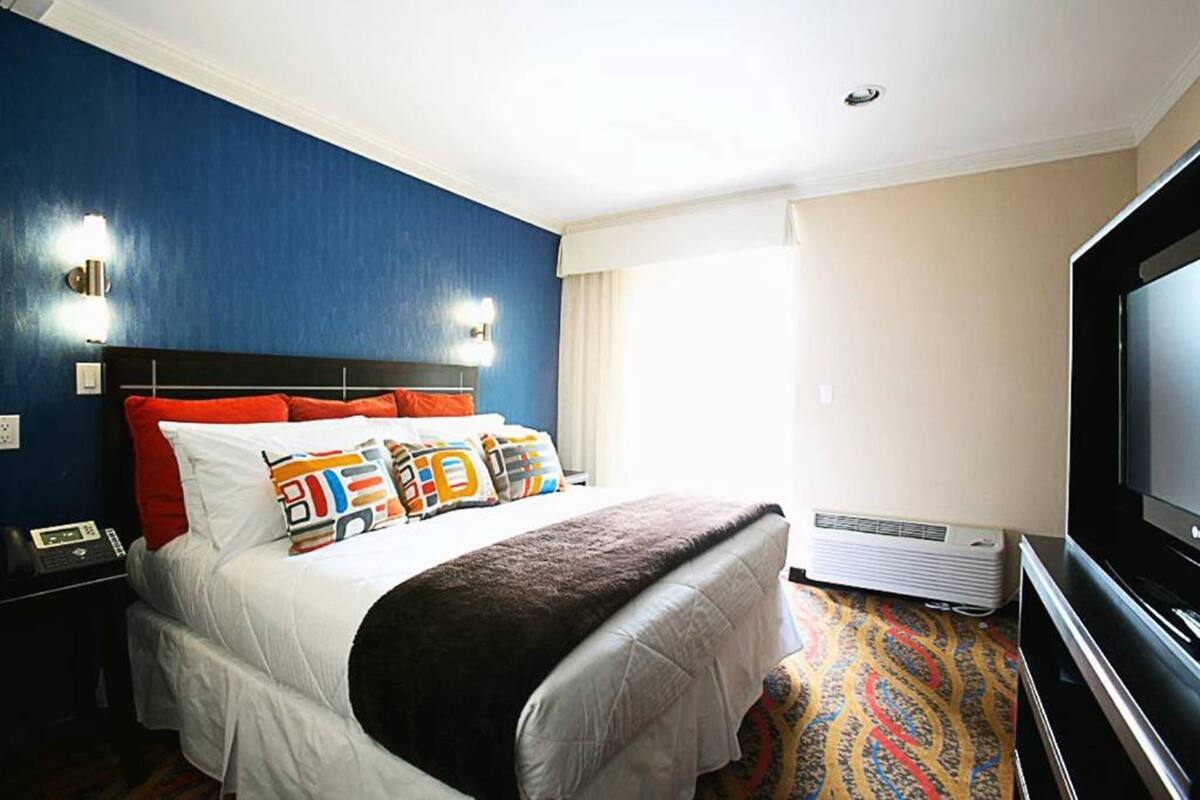 Quarto de hotel com cama, televisão, ar condicionado e mesa de cabeceira.