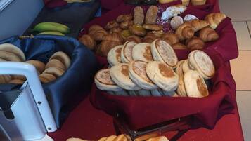 Buffet com diversos alimentos, incluindo pão, doces e frutas.