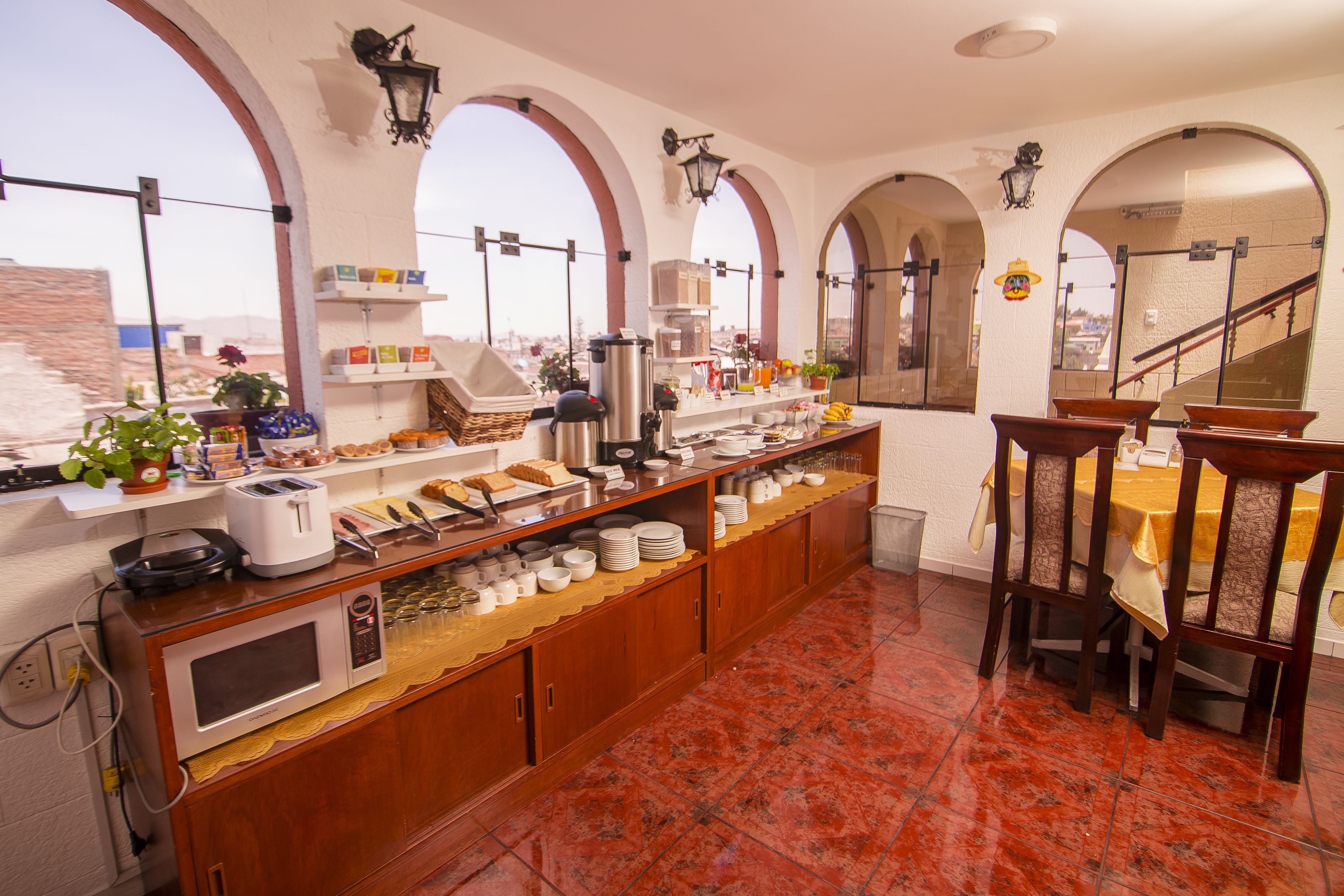 Um buffet de café da manhã com diversas opções de comida, micro-ondas e área de estar com cadeiras e mesa.