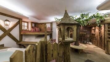Interior rústico com vigas de madeira, uma cama em mezanino, cerca de madeira e uma pequena estrutura semelhante a uma casinha na árvore.