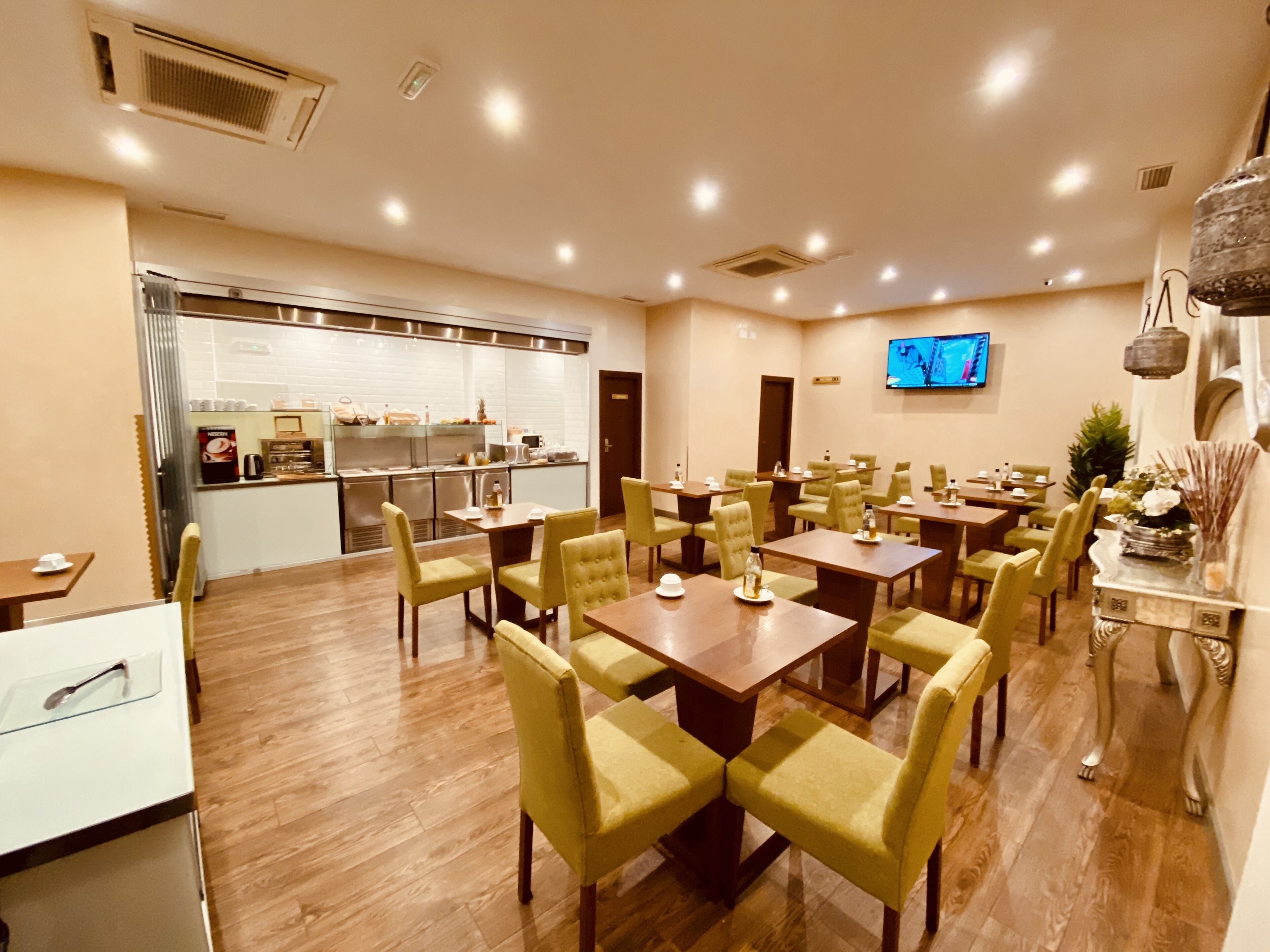Um restaurante com várias mesas e cadeiras, uma área de cozinha e uma televisão na parede.