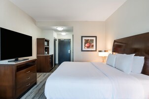 Quarto de hotel com uma cama grande, televisão de tela plana, escrivaninha com computador e quadro pendurado na parede.