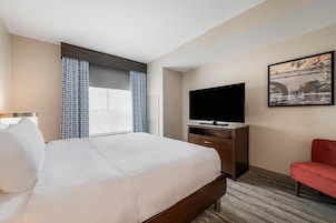 Quarto de hotel com cama, televisão, escrivaninha e uma cadeira.