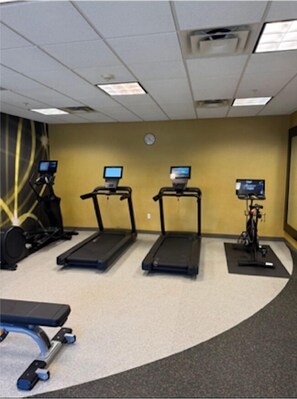 Uma sala de ginástica com esteiras, bicicleta ergométrica e um banco.