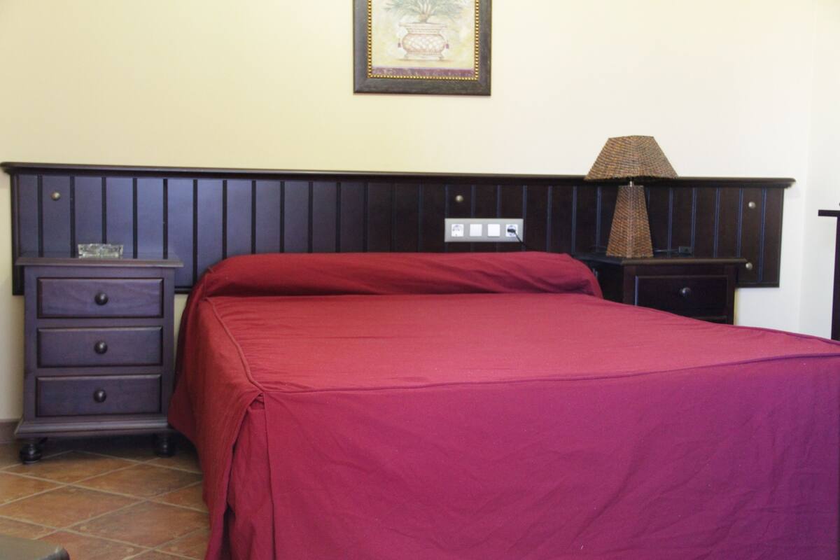 Quarto com cama, mesa de cabeceira, abajur e cômoda.