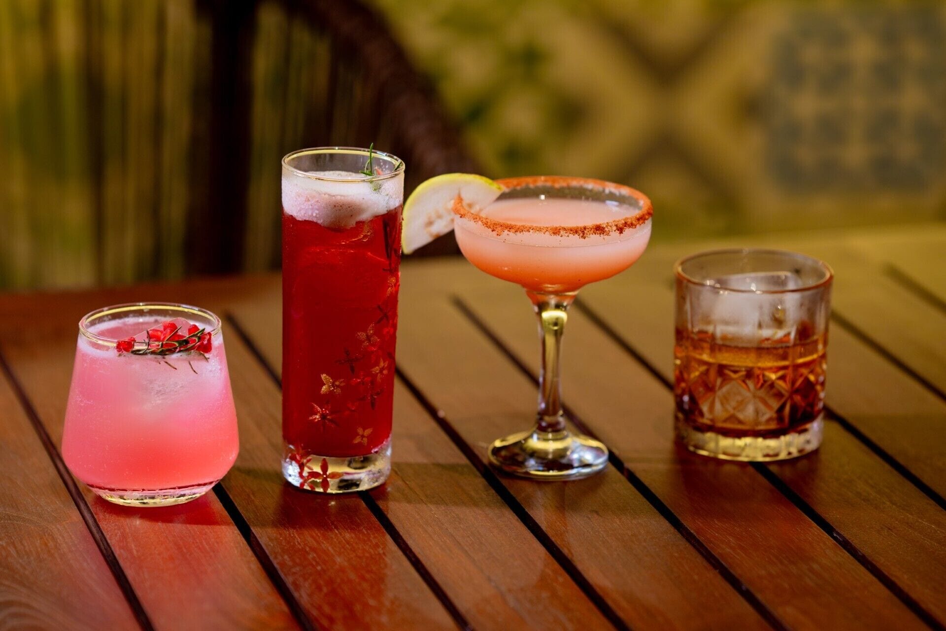 Quatro copos com bebidas diferentes sobre uma mesa de madeira.