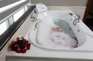 Uma banheira com pétalas de rosa e uma vela acesa, um controle digital de temperatura da água e uma toalha branca na borda.
