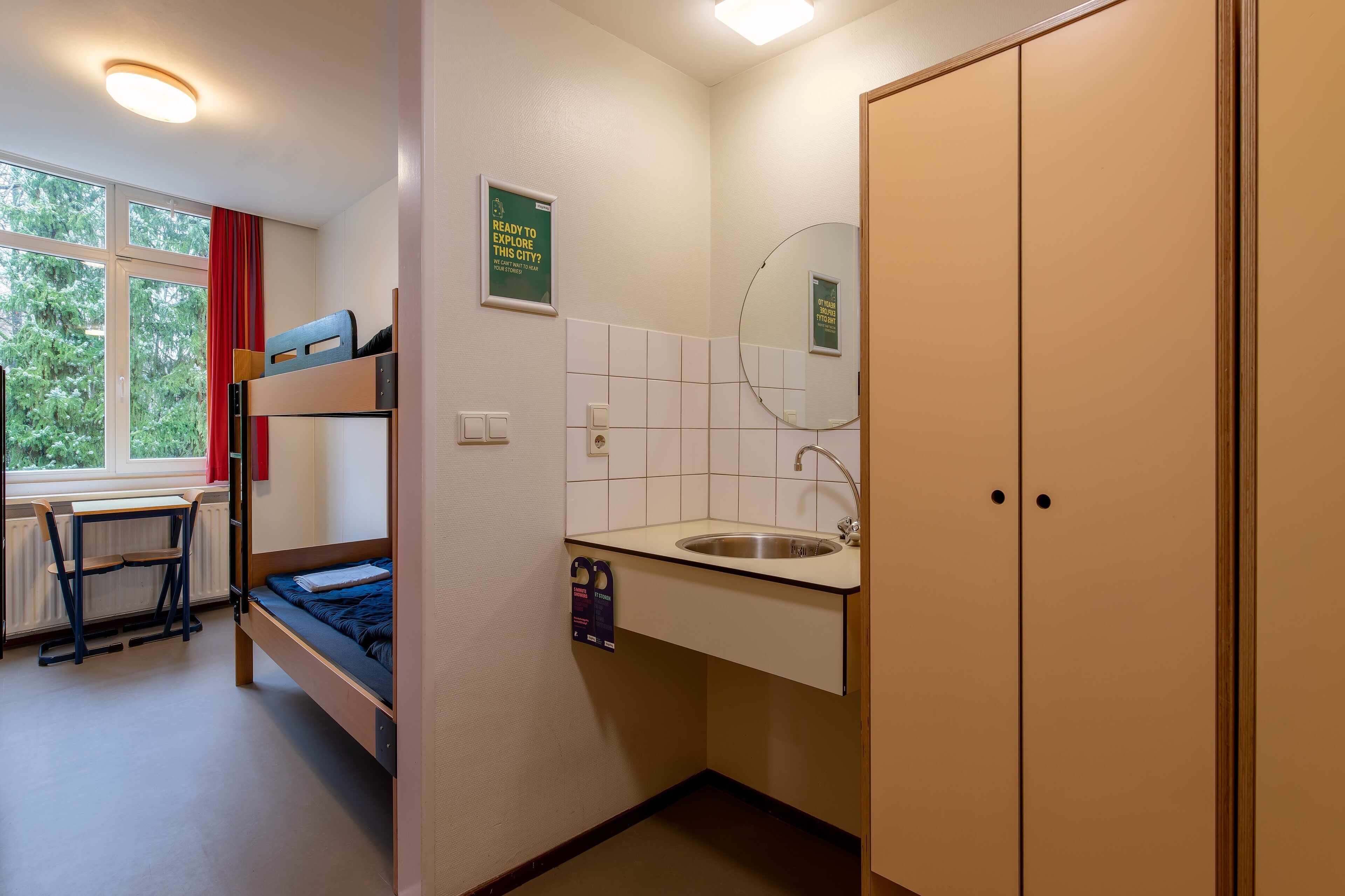 Quarto de dormitório com beliches, escrivaninha, pia e espelho.