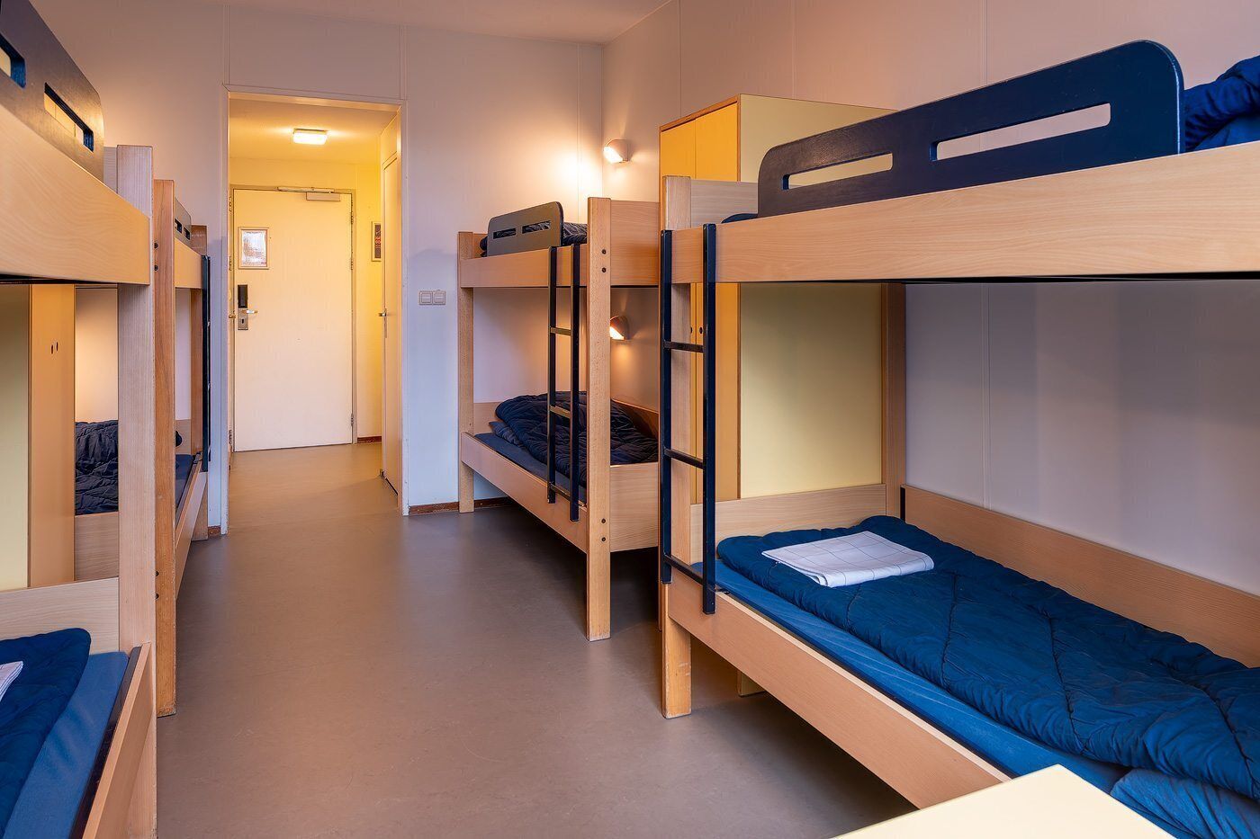 Quarto de dormitório com beliches, piso de madeira e porta que dá para outro cômodo.