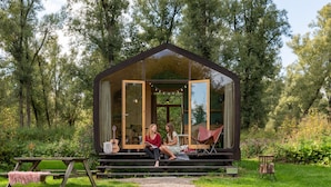 Uma cabana com teto de vidro e deck de madeira, rodeada por vegetação exuberante.