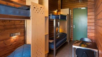 Uma cabana com beliches, uma escrivaninha e uma porta verde.