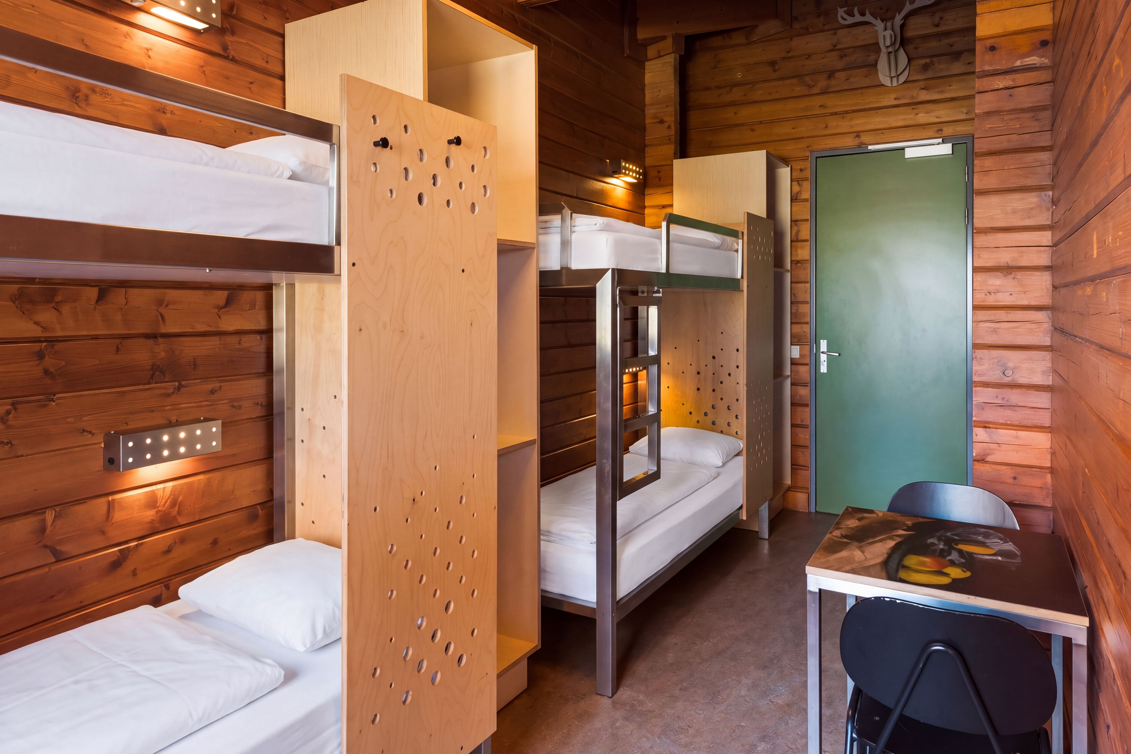 Quarto com beliche, escrivaninha, cadeira, paredes de madeira e porta verde.