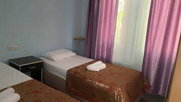 Quarto de hotel com duas camas, uma mesinha de cabeceira e uma janela com cortinas roxas.