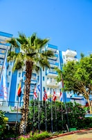 Um hotel com fachada azul e branca, palmeiras e várias bandeiras.