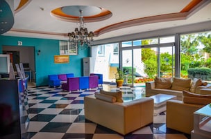 Um hall de hotel com chão quadriculado, um candelabro e uma grande janela com vista para áreas verdes e edifícios.