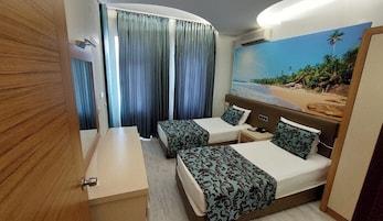 Quarto de hotel com duas camas, uma escrivaninha e um grande mural de praia na parede.