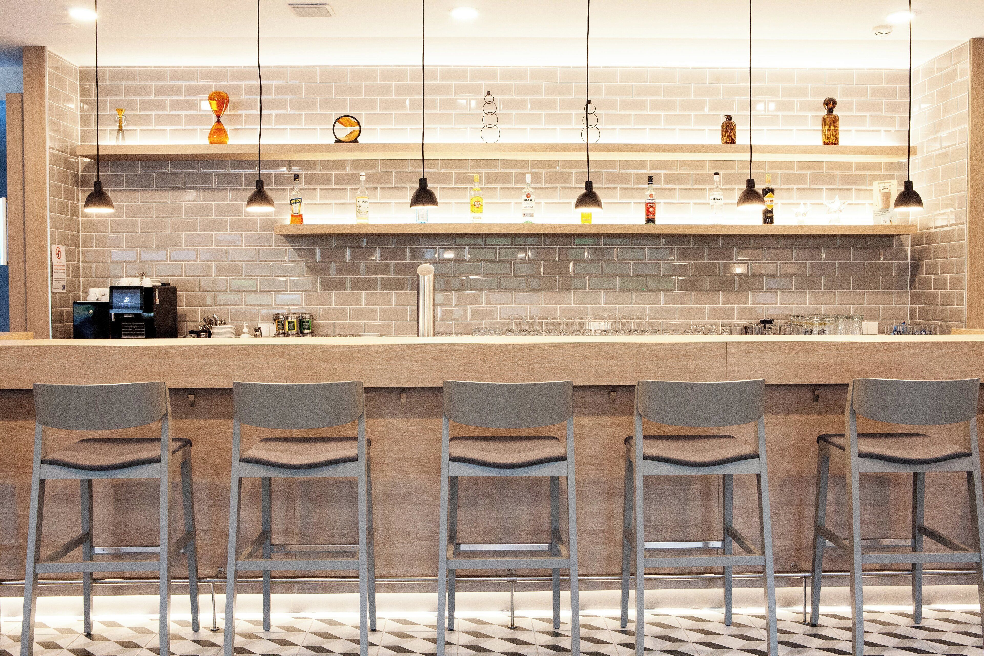 Uma área de bar moderna com painel de azulejos, iluminação pendente e banquetas.